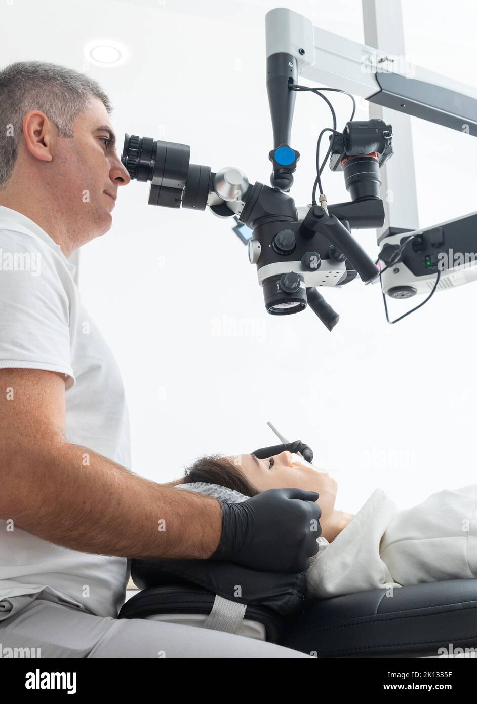 Dentist using dental microscope treating patient teeth at dental clinic ...