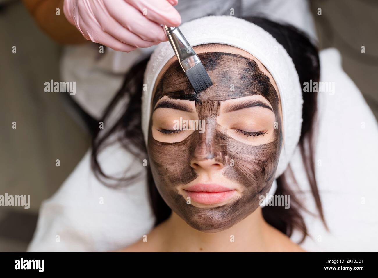 cosmetologist applying black mask on pretty woman face wearing black ...