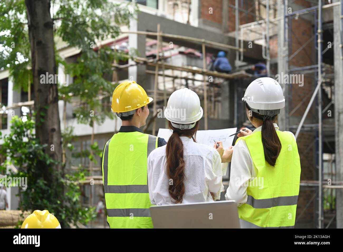 Rear view of inspectors team in safety helmet working with blueprints ...