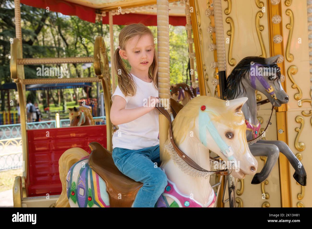 Little girl in a white t-shirt rides a carousel in an amusement park ...