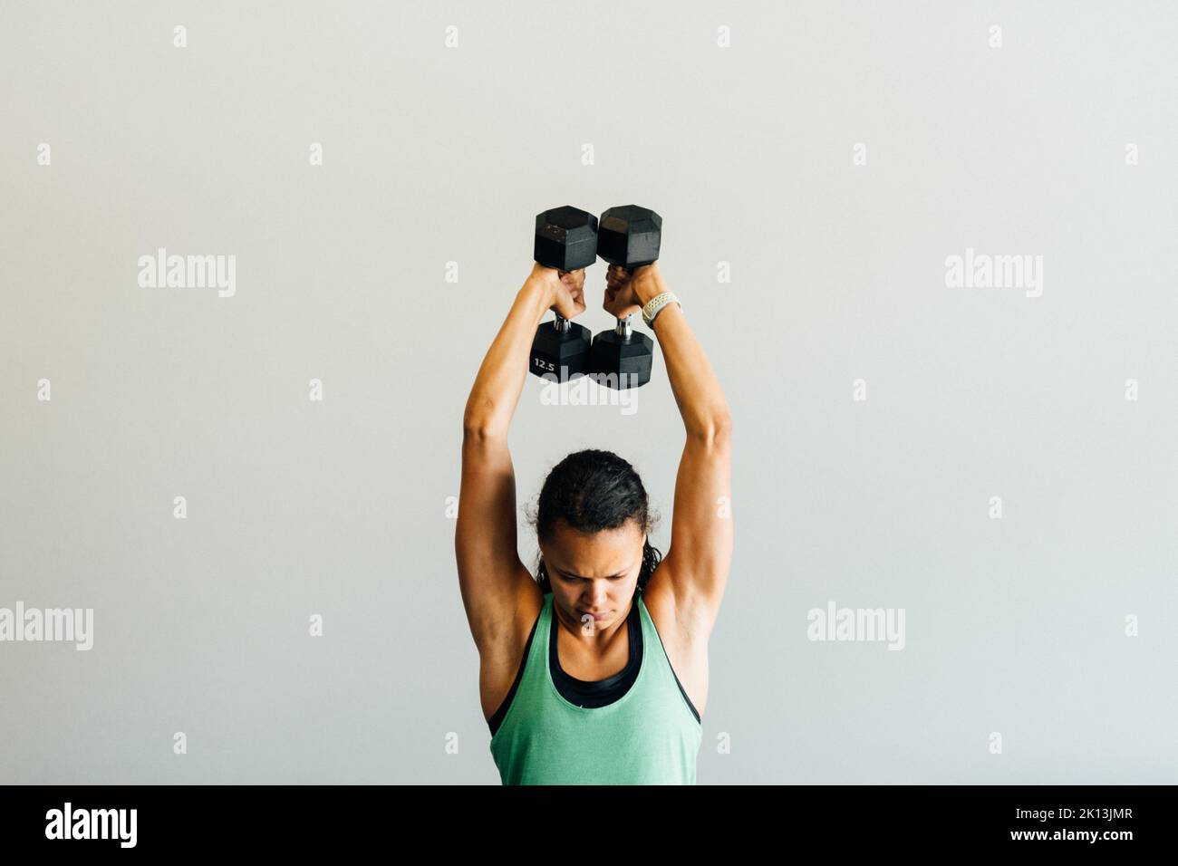 A fit African American female working out with weights on a white wall ...