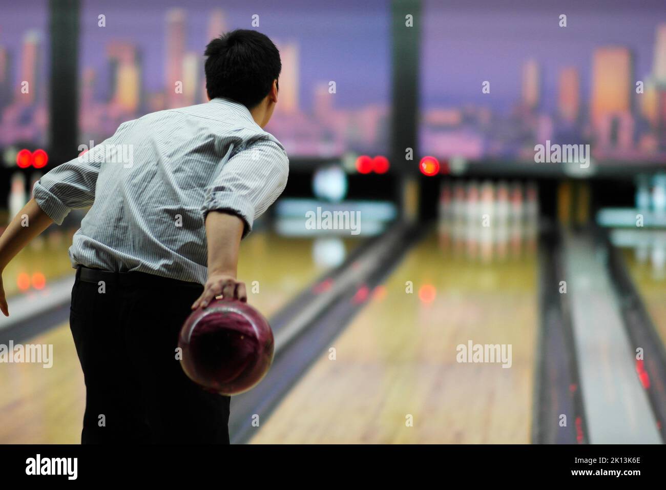 A back view of a young man in a shirt and trousers playing bowling ...