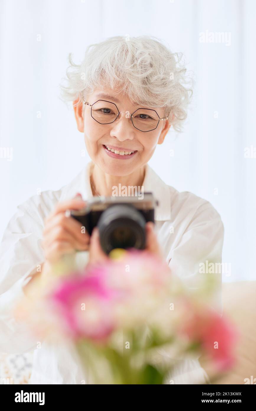 Japanese senior woman taking pictures of flowers on the sofa Stock ...