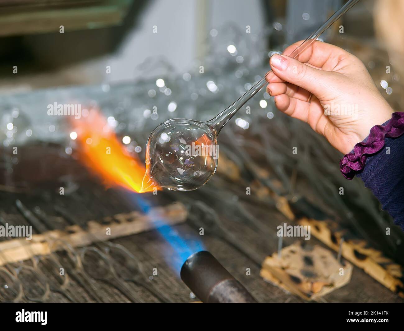 Glassblower heats the glass piece for shaping the future Christmas ...