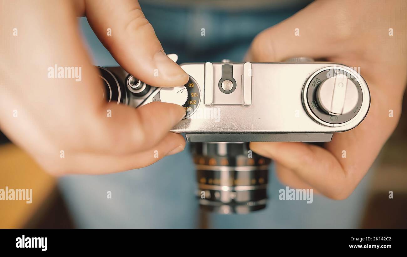A young photographer changes shutter speed of a vintage old film camera ...