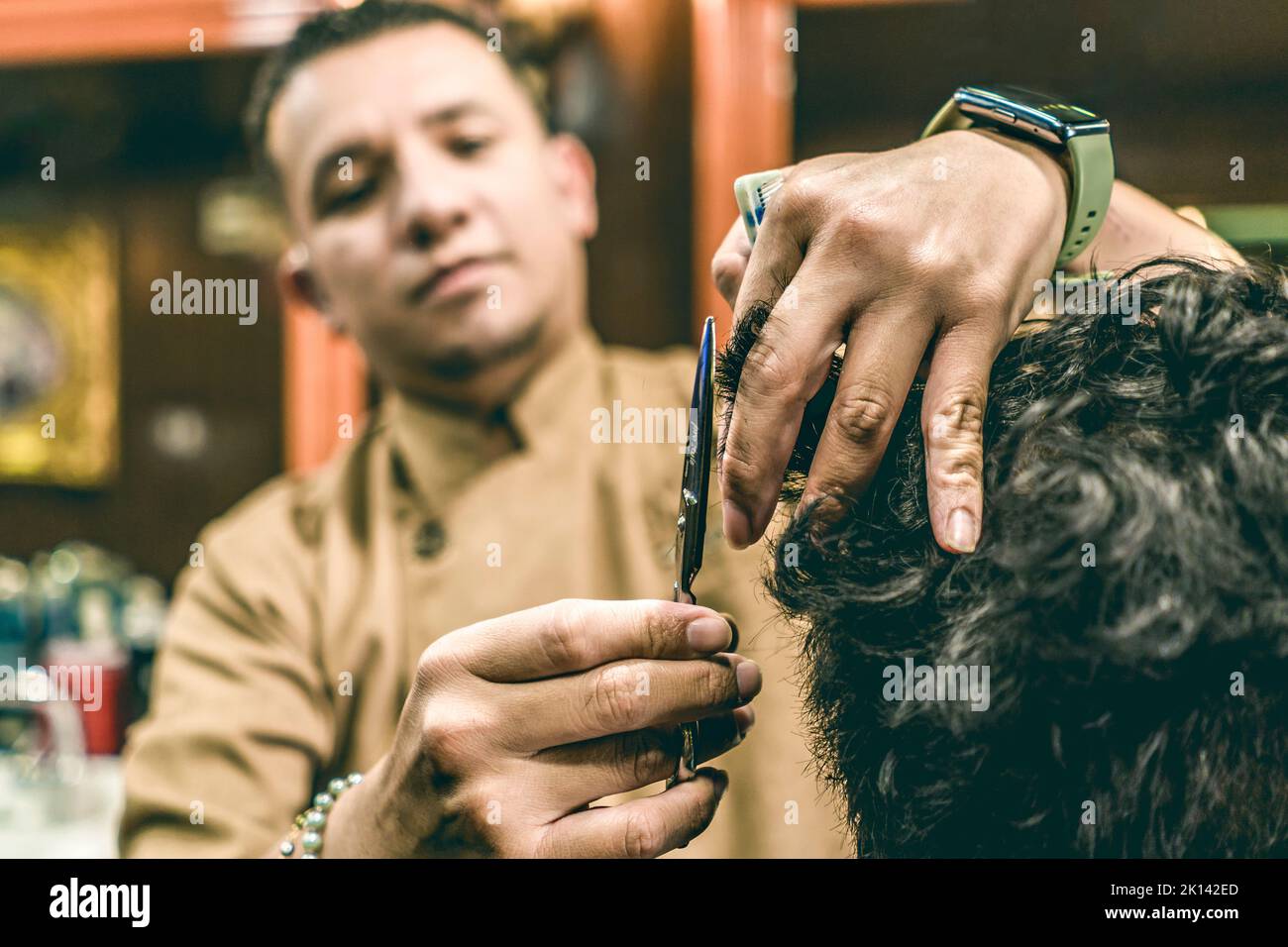 Out of focus young barber holding sharp professional scissors cuts hair ...