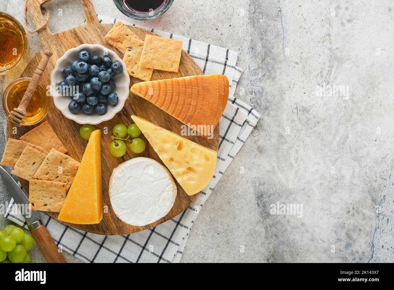 Assortment of cheese, honey, cracker, blueberries, grapes with red and ...