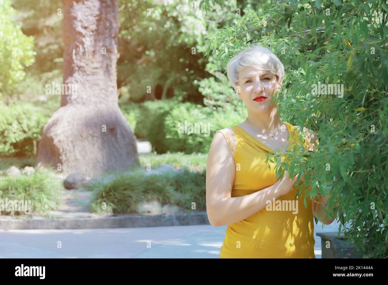 A beautiful woman is photographed with a green bush in park. The ...