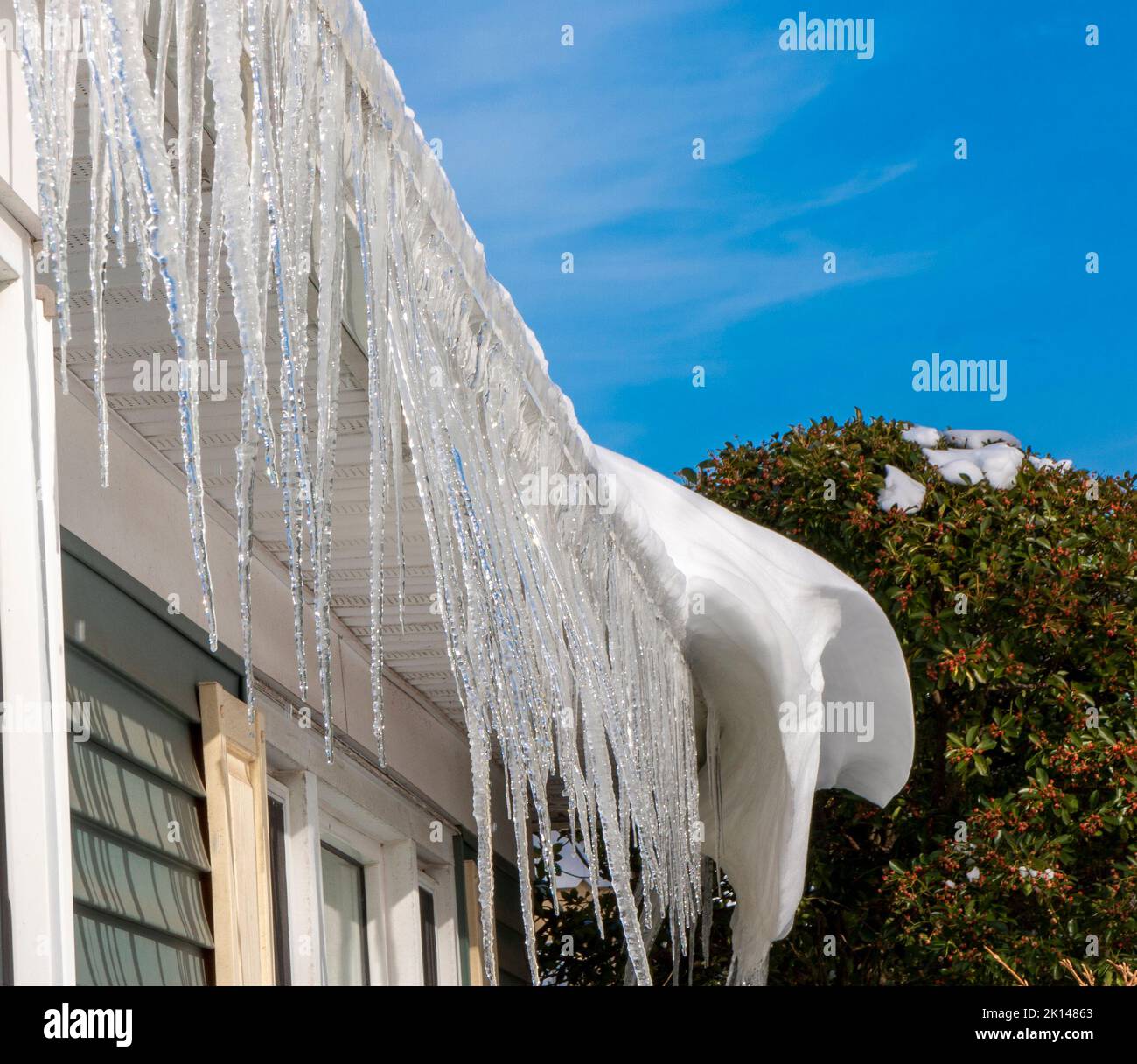 a few days after a snow storm icicles hanging from roof of a house as the snow is melting with ...