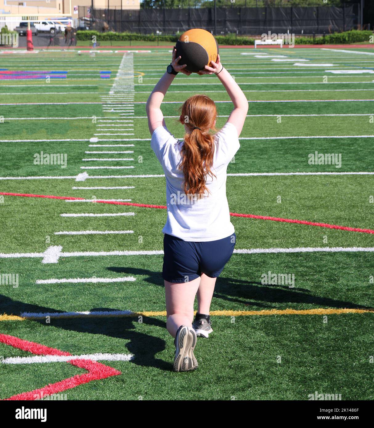 Rear view of a young female athlete holding a medicine ball overhead ...