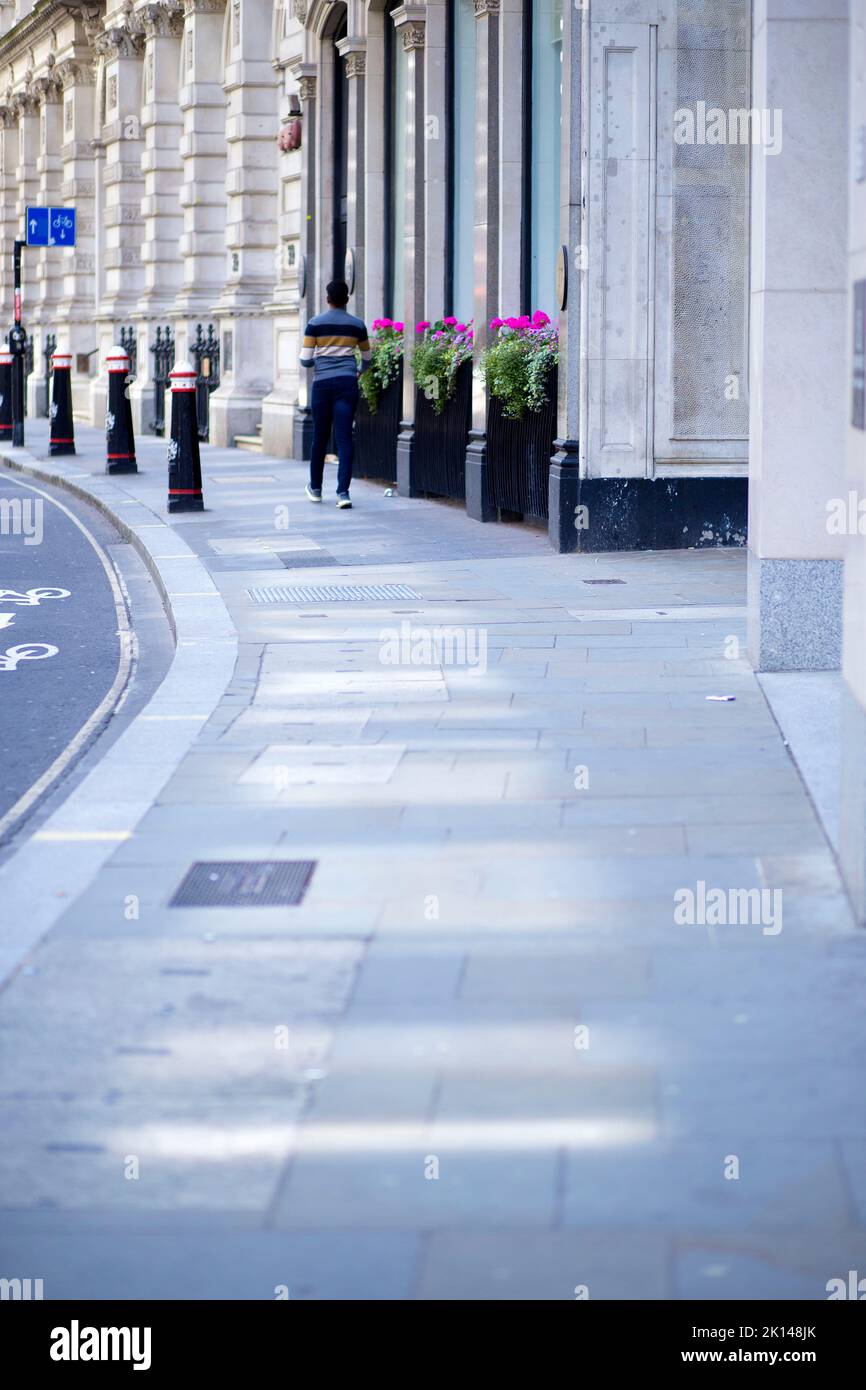 Lights of reflection fall on a pavement as a pedestrian walks in the ...