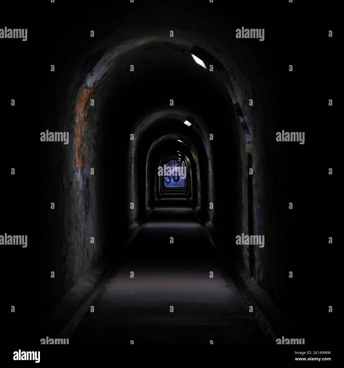 A dark narrow tunnel hallway leading to blue light Stock Photo - Alamy