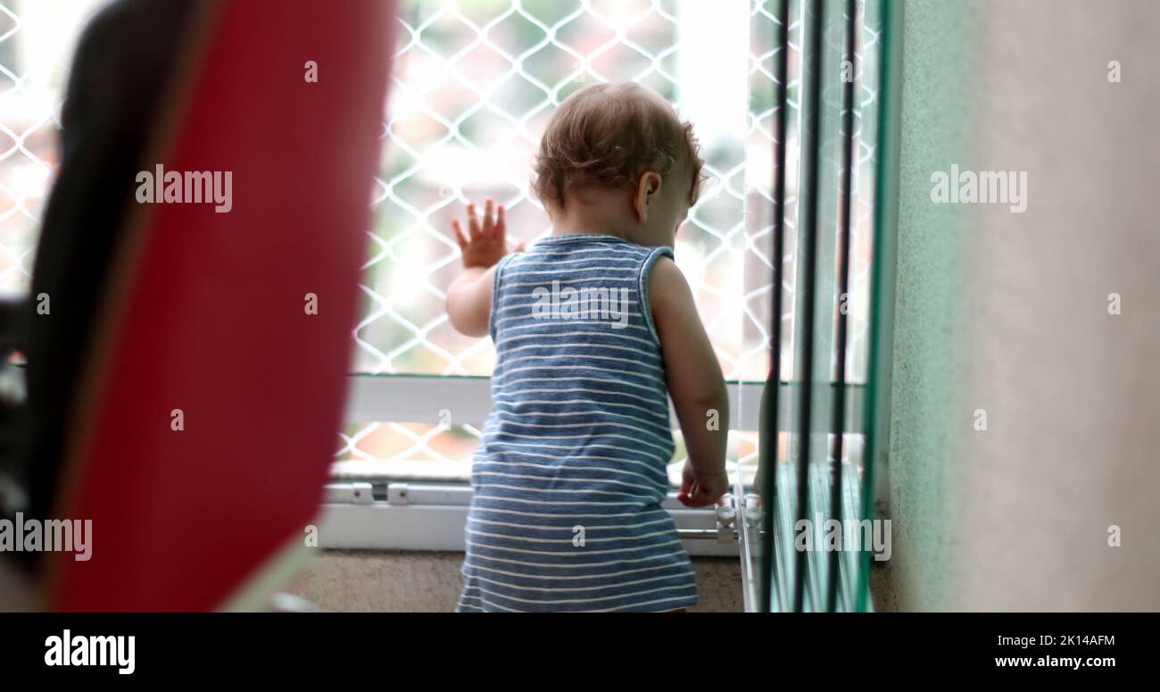 Cute baby standing by apartment window exploring home during lockdown ...