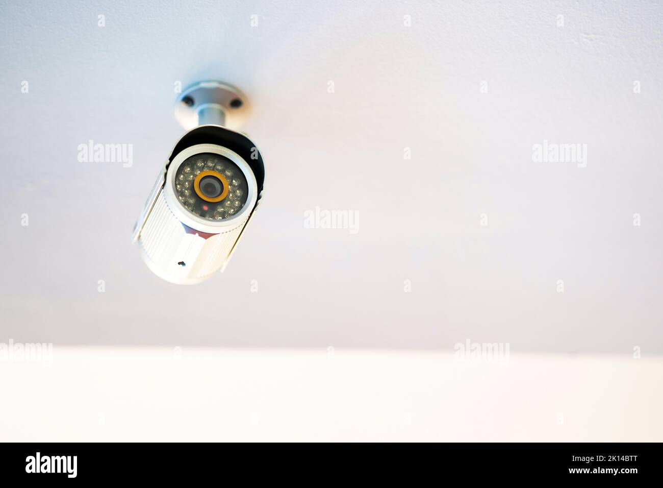 White CCTV with orange black camera len in the centre hanging from the ...