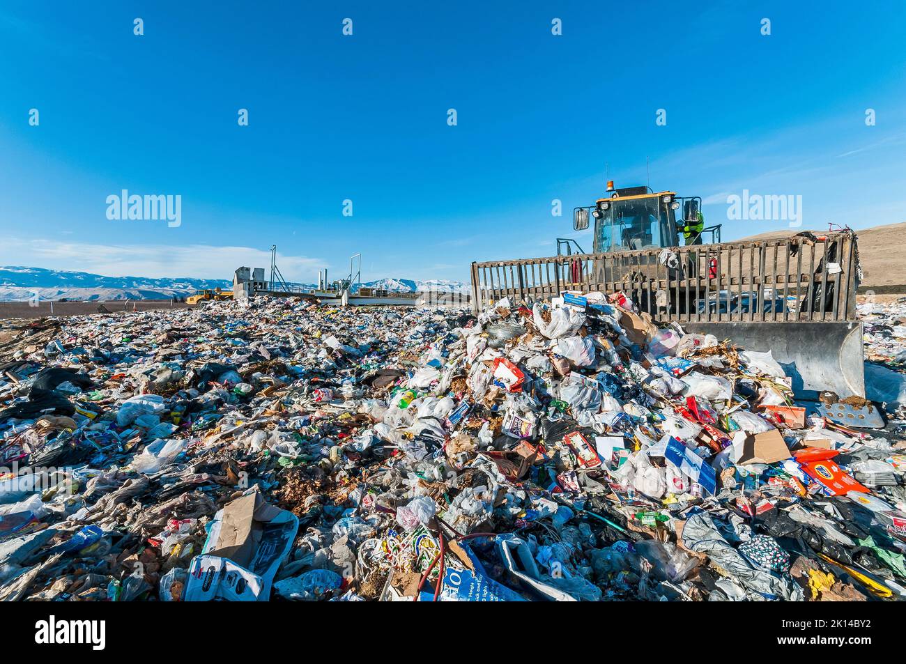 A soil compactor bulldozer pushing solid waste at an active landfill ...