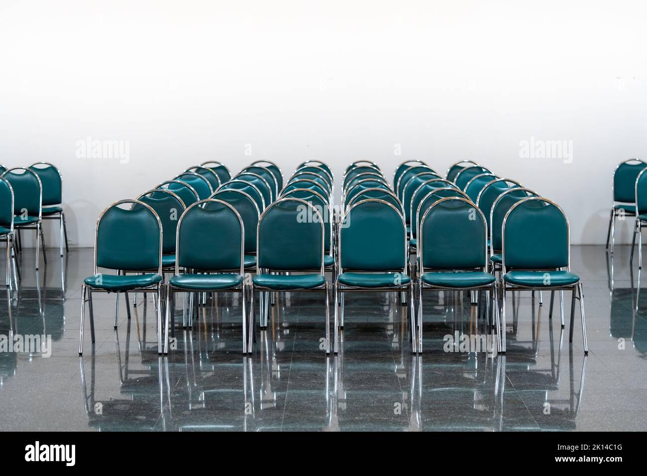 Many empty green leather chairs in a wide hall room, lights on. A floor ...