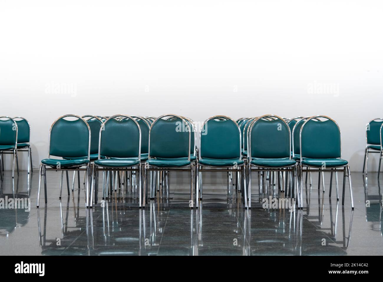Many empty green leather chairs in a wide hall room, lights on. A floor ...
