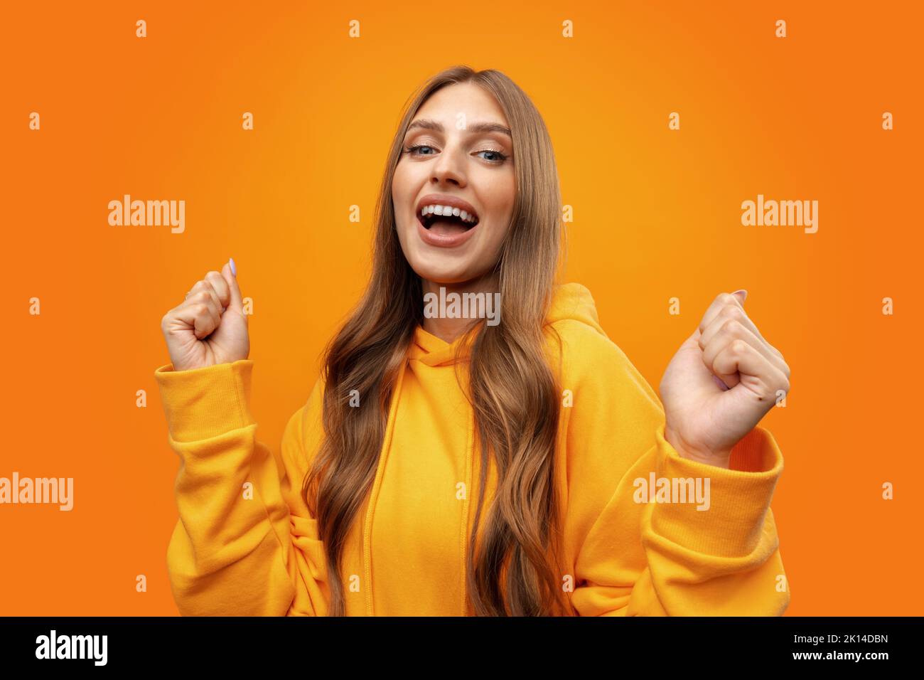 Portrait of an excited young woman celebrating success with raised arms ...