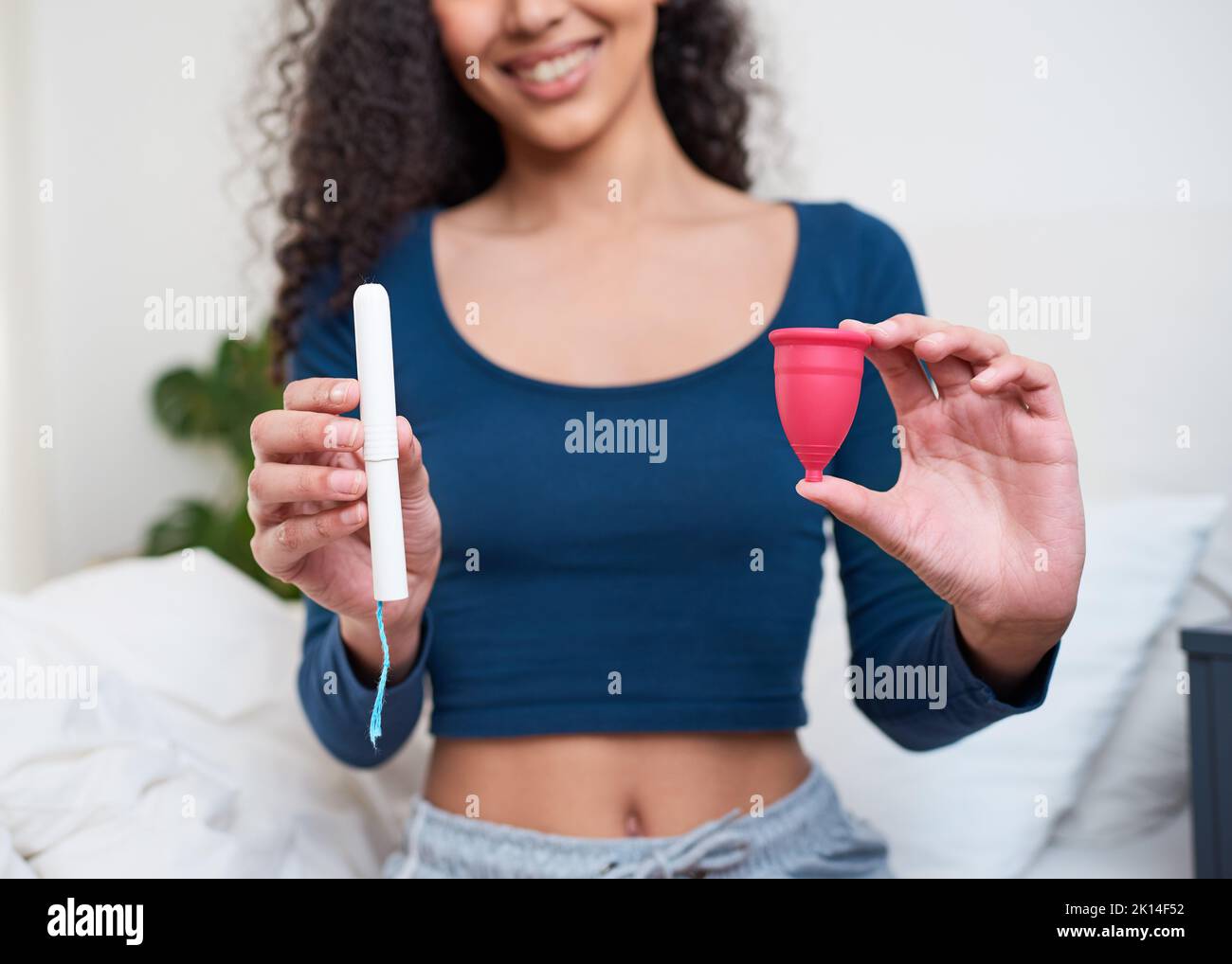 A young multi-ethnic woman holds tampon and menstrual cup for ...