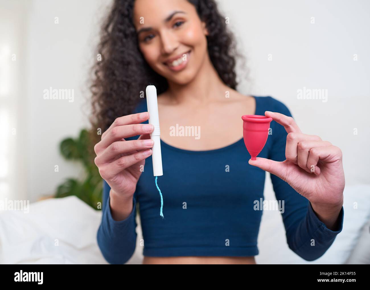 A young multi-ethnic woman holds tampon and menstrual cup for ...