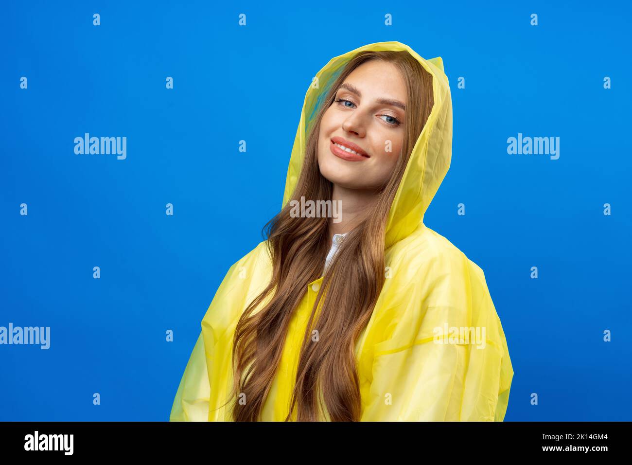 Young blonde woman wearing yellow raincoat smiling at camera over blue ...
