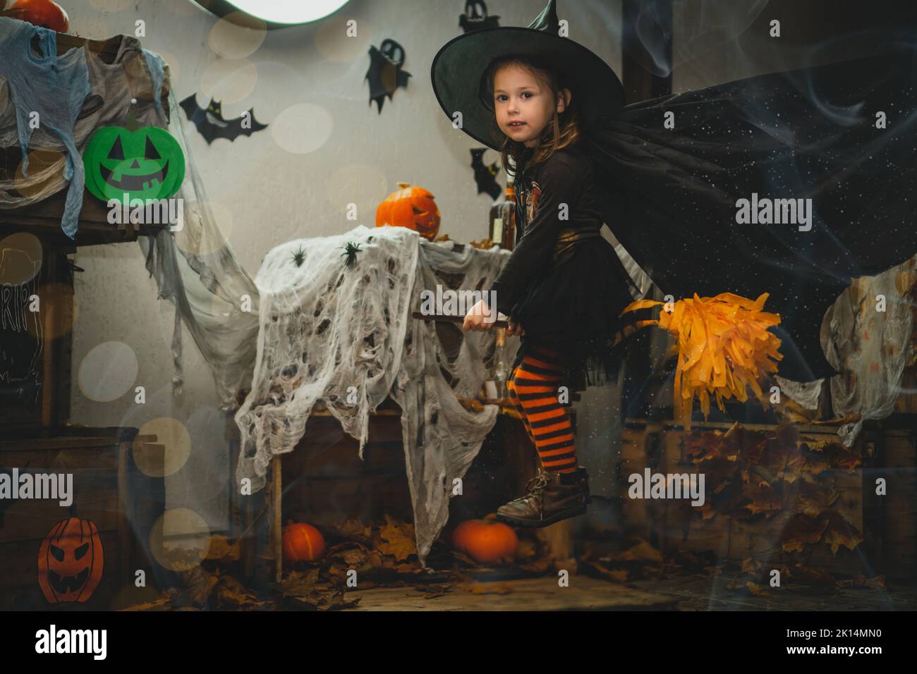 Little girl 3-4 years old in witch costume and striped stockings flies ...