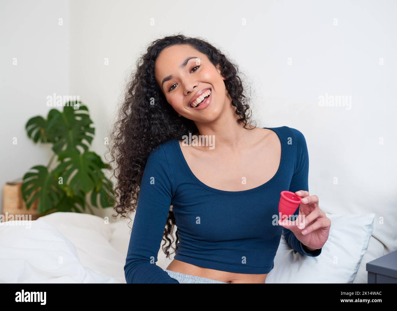 A young multi-ethnic woman holds menstrual cup and looks happy sitting ...