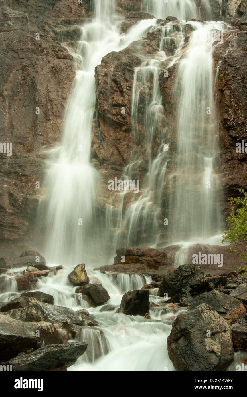 A vertical shot of a scenic waterfall coming over a rocky hill in the ...