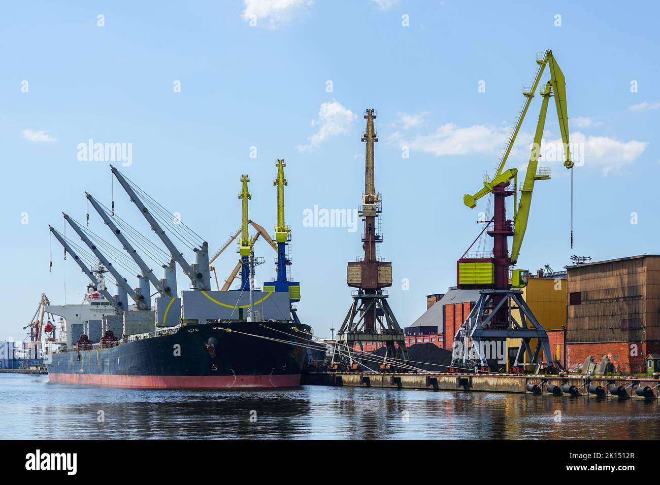 Large bulk carrier with open holds in harbor quay, shore cranes and ...