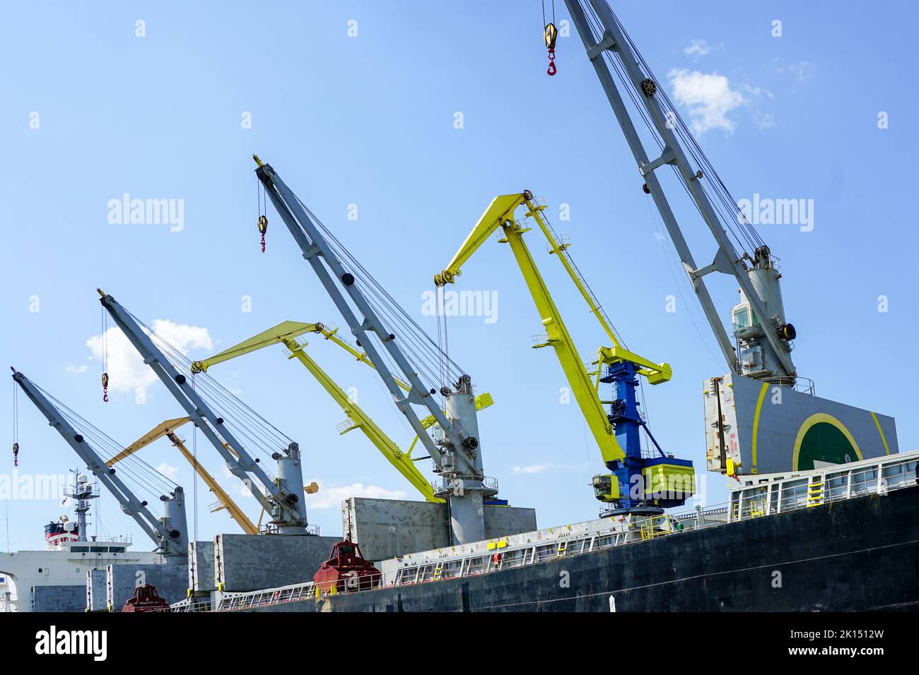 Large bulk carrier with open holds in harbor terminal, shore cranes and ...