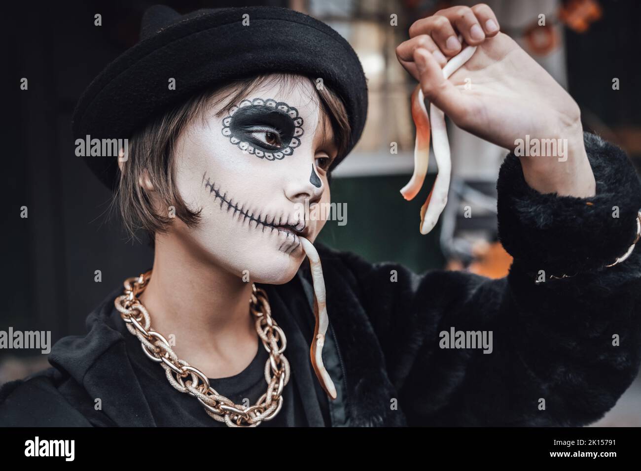 Beautiful scary little girl celebrating halloween, chewing gummy worm ...