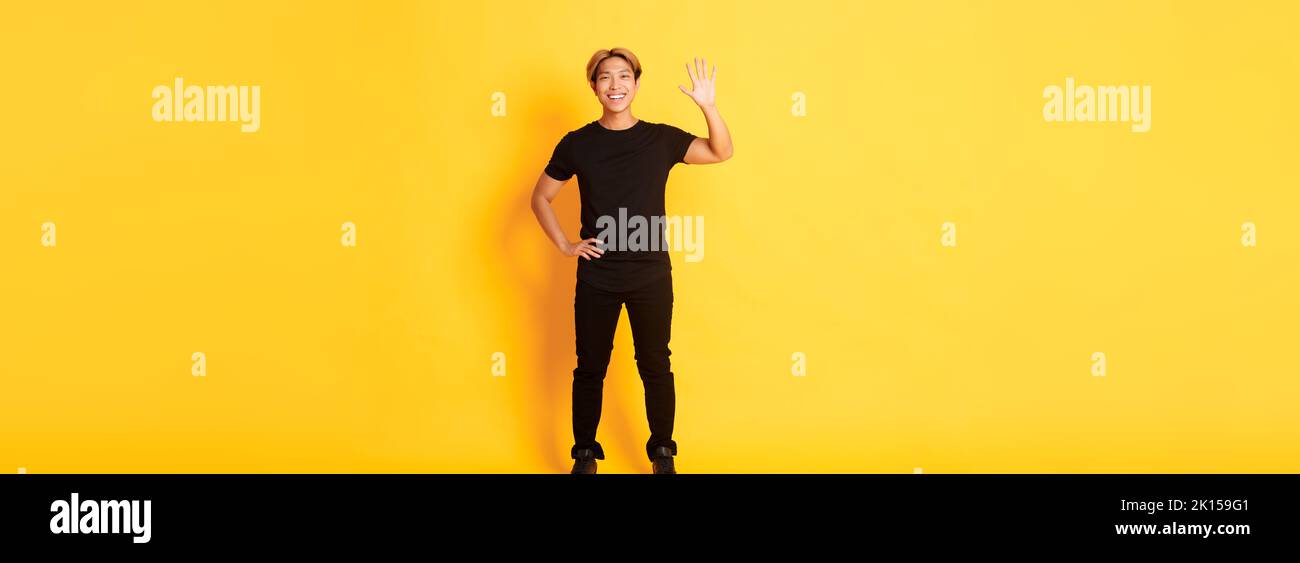 Full-length of friendly handsome asian man waving hand in hello ...