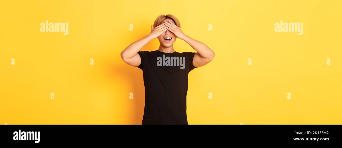 Portrait of amused and excited smiling blond guy shut eyes with palms ...