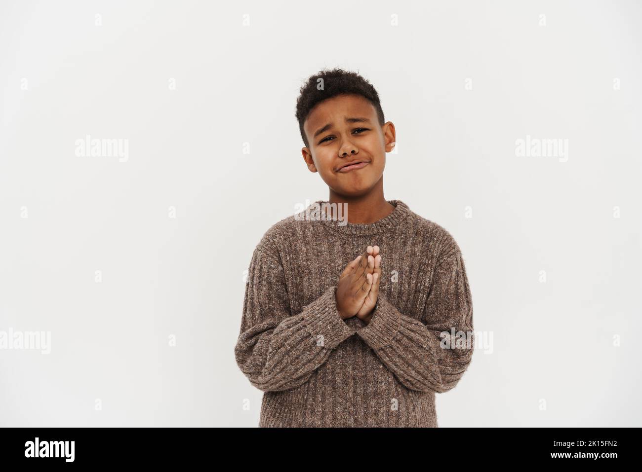 Black preteen boy wearing sweater crying while making prayer gesture ...