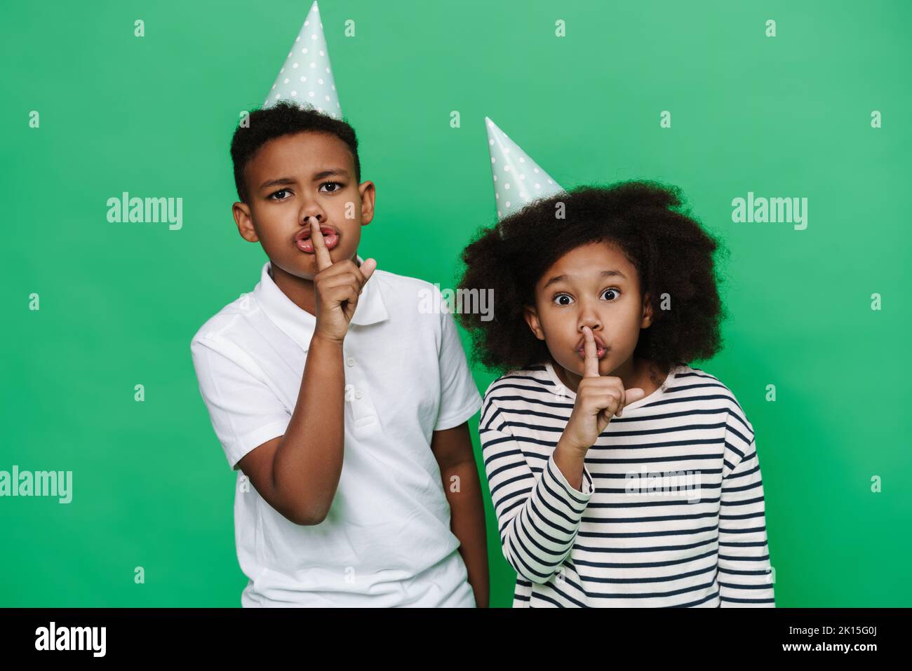 Black boy and girl wearing party cones making silence gesture together ...