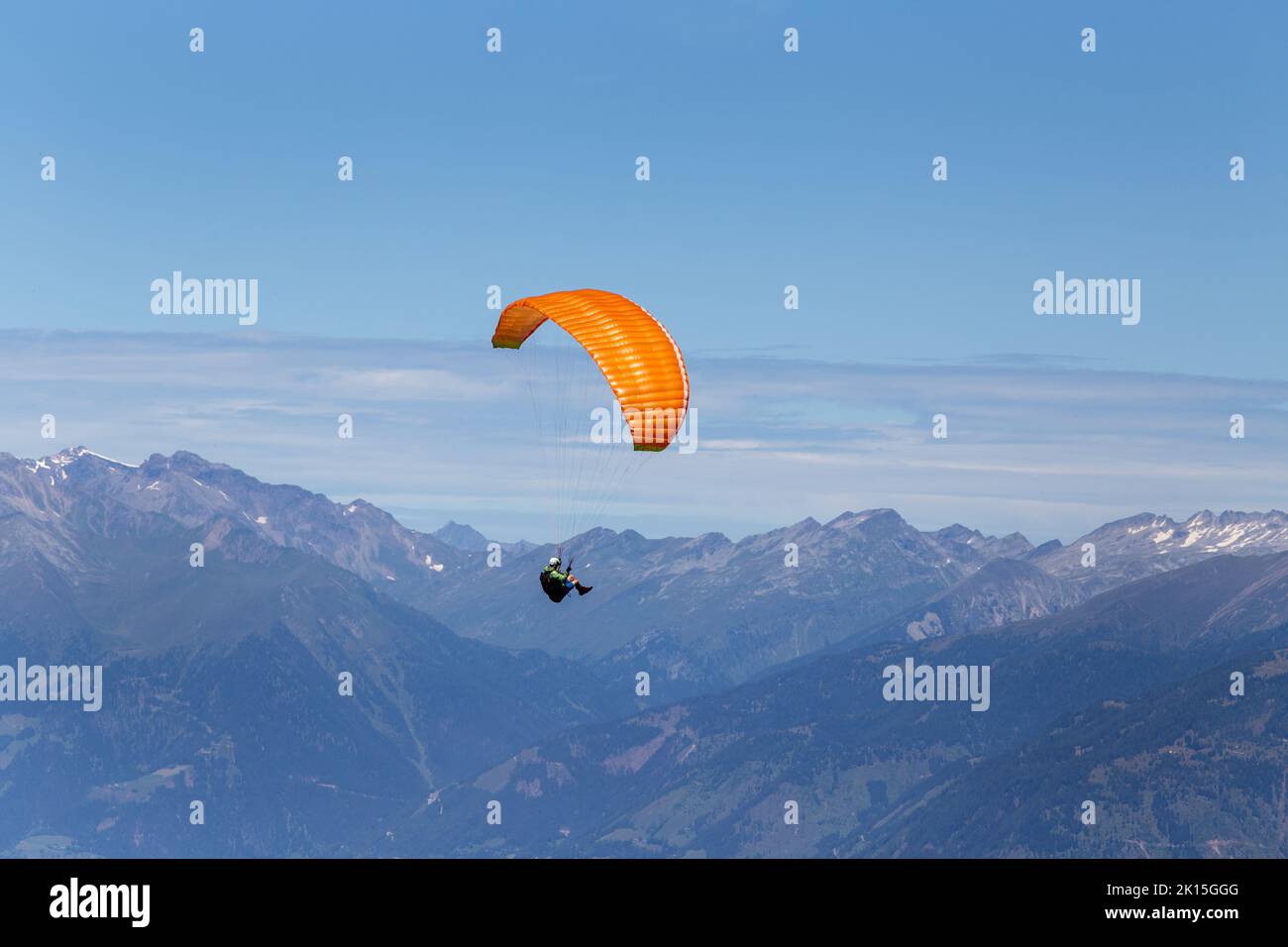 Man with parachute flying above mountain peaks of austrian alps in ...