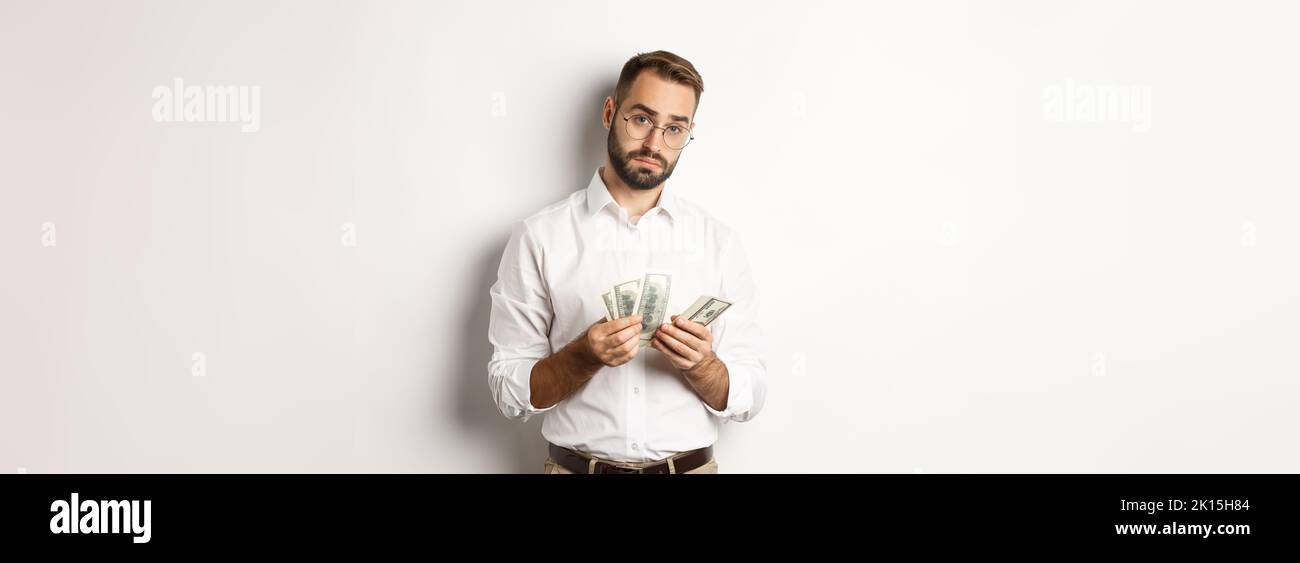 Handsome businessman counting money and looking at camera, standing ...