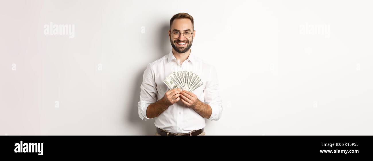Smiling handsome man holding money, showing dollars, standing over ...