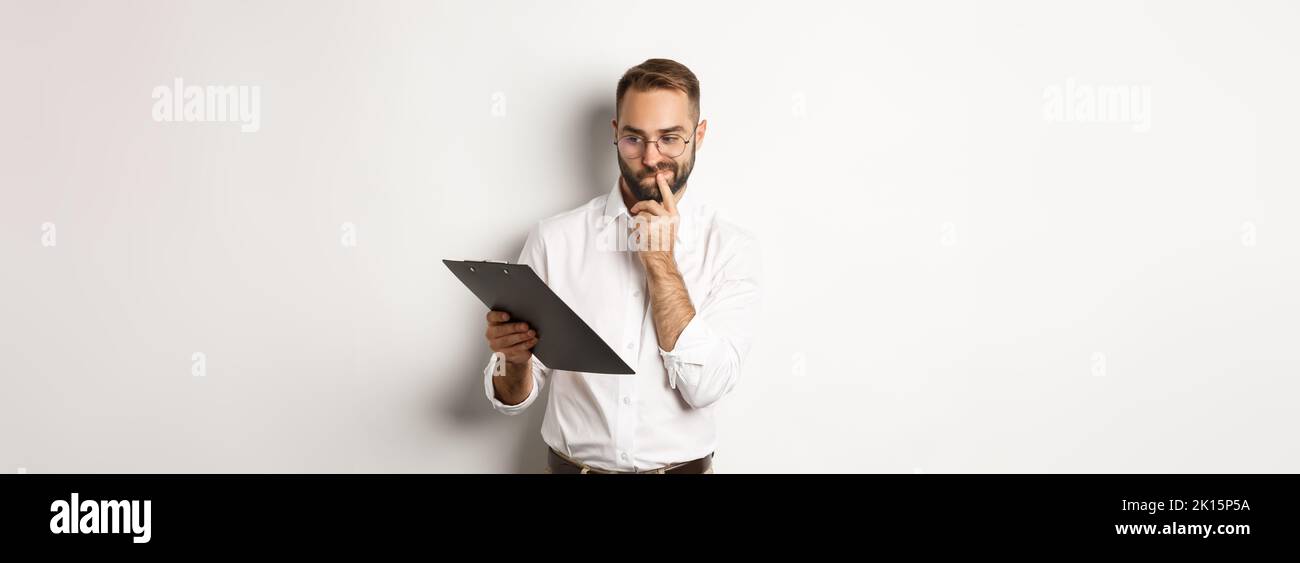 Thoughtful employee looking at clipboard, having doubts, standing over ...