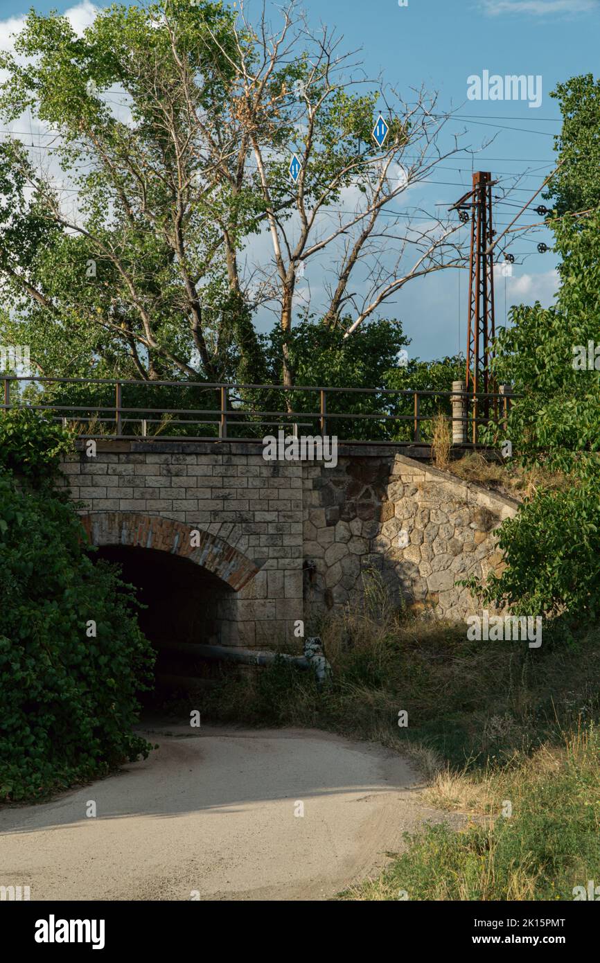 A vertical landscape of a tunnel under a stone bridge with greenery ...