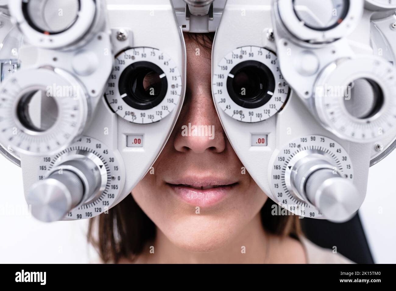 Smiling female patient in modern phoropter checking vision during visit ...