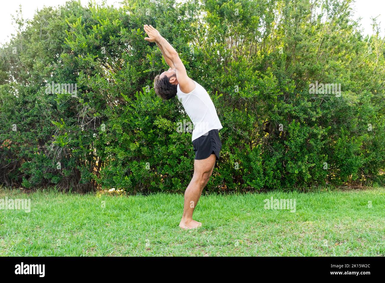 Side view of barefoot male in activewear raising arms and bending back ...