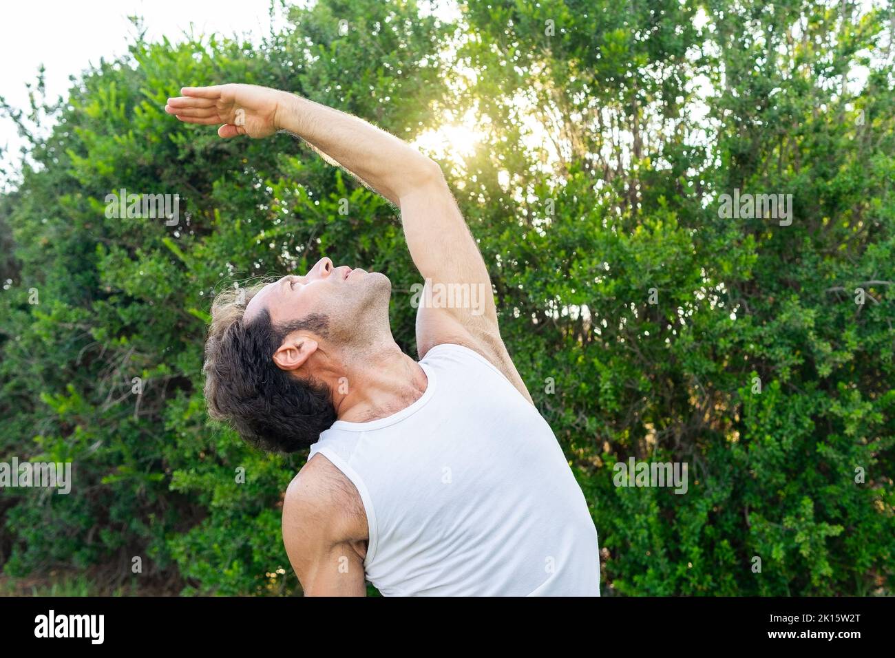 Mature man in activewear raising arm and bending back while doing ...