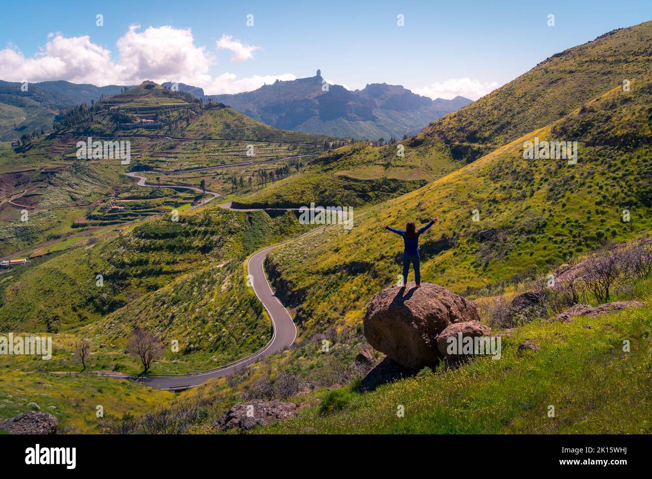Back view of female adventurer standing with spread arms on rock in ...