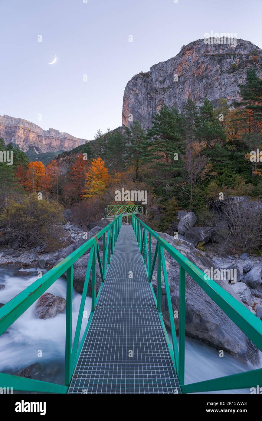 Narrow footbridge crossing fast mountain river in autumn evening sunset ...