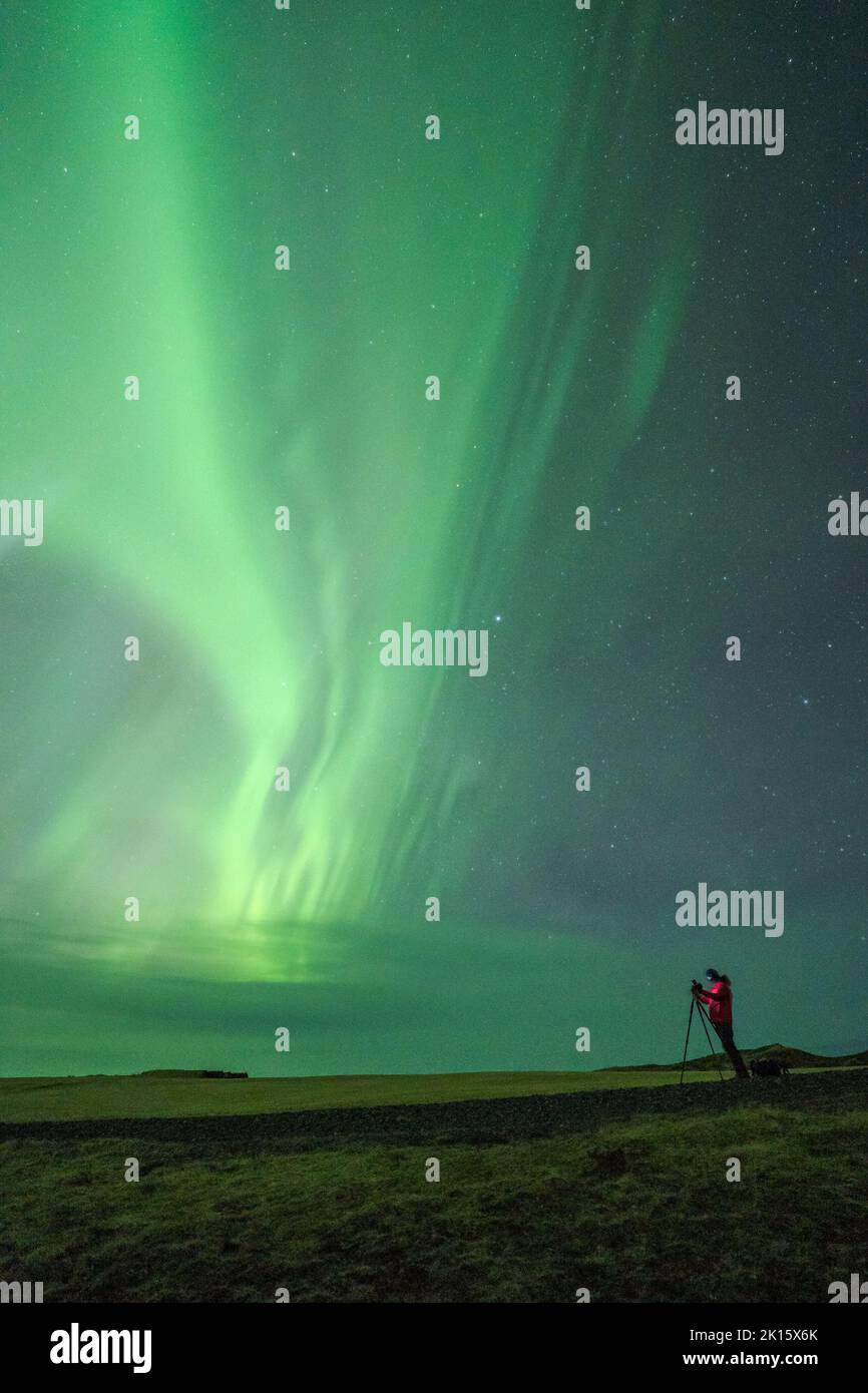 Remote view of unrecognizable traveling photographer taking picture of green aurora borealis ...