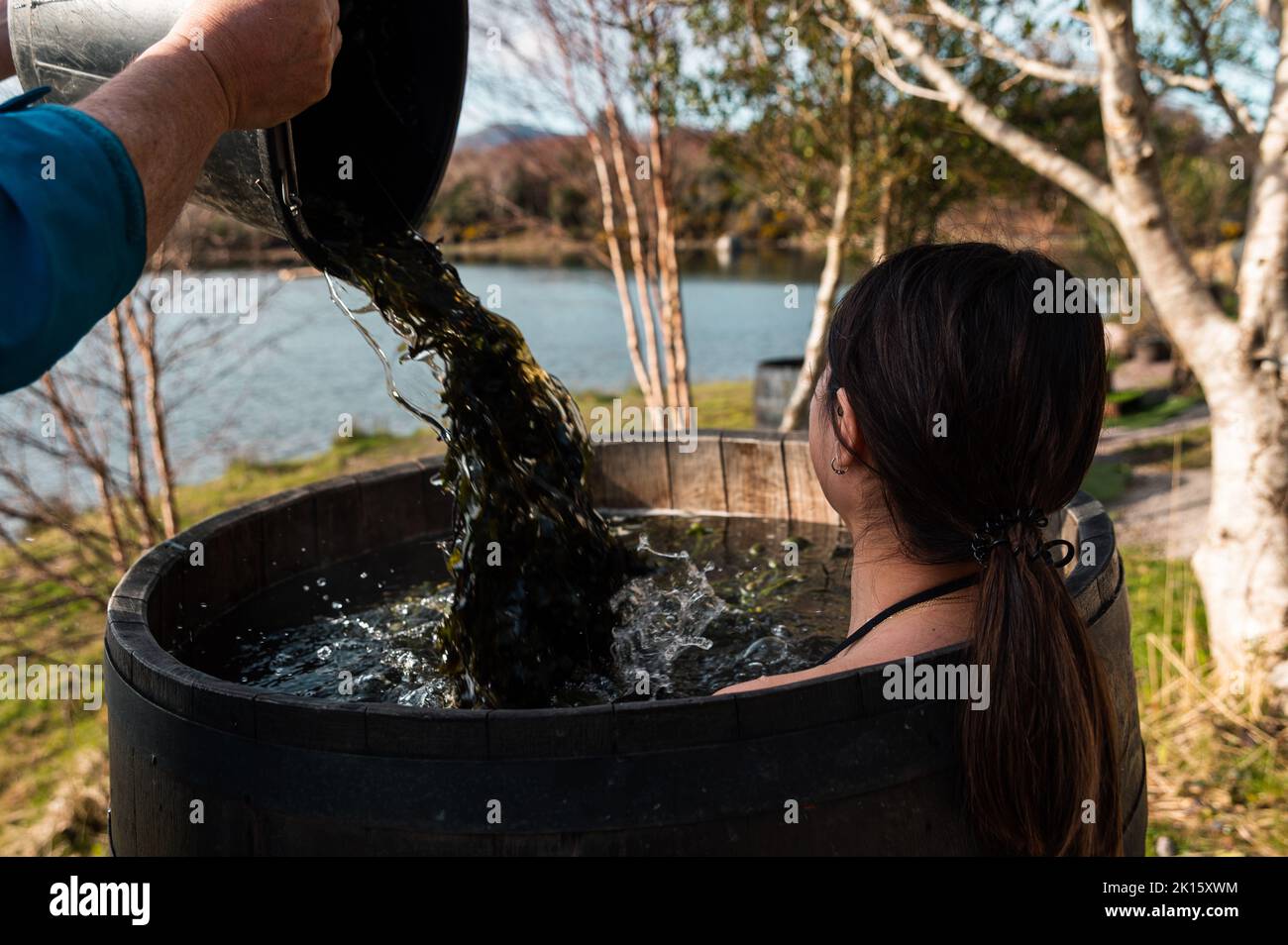 Crop male pouring water with algae into wooden barrel with brunette ...