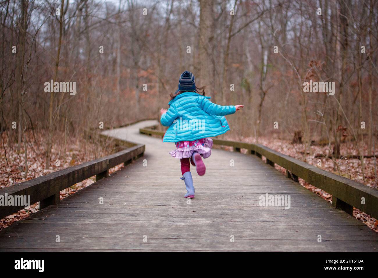 A child in bright colorful clothes runs down path in woods Stock Photo ...