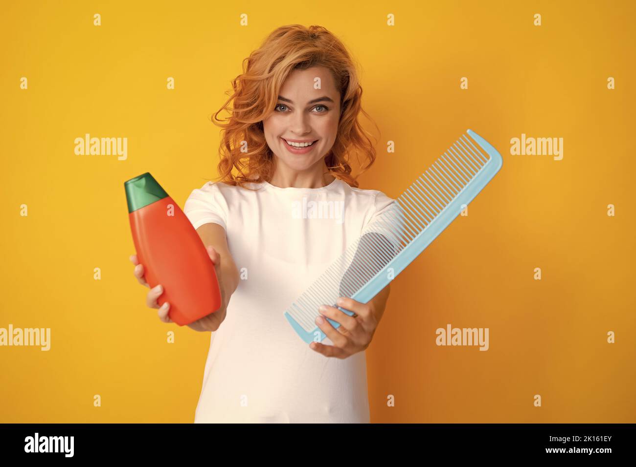 Funny portrait of redhead woman with a comb, isolated on yellow ...