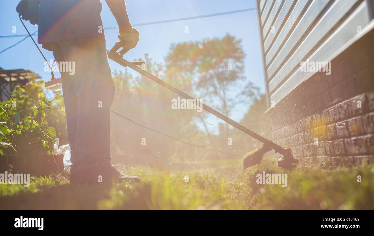 Man mowing tall grass with electric or petrol lawn trimmer in backyard ...